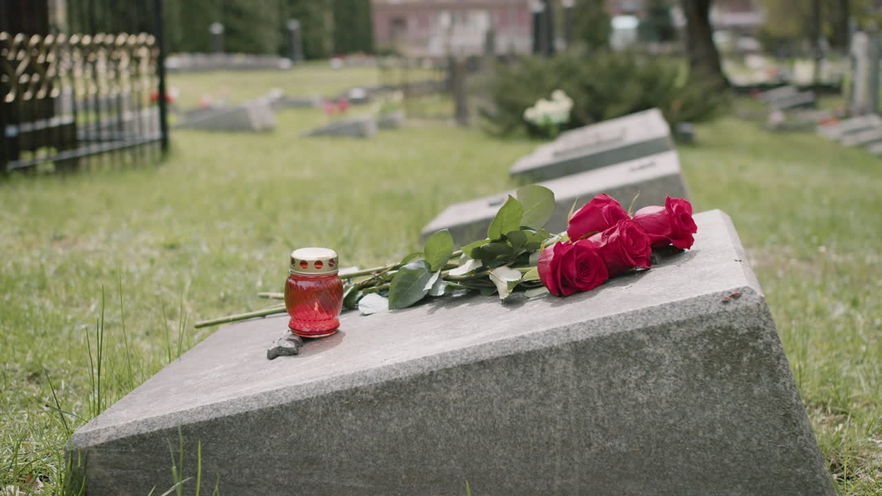 Premium stock video - Side view of red roses and a candle on tombstone ...