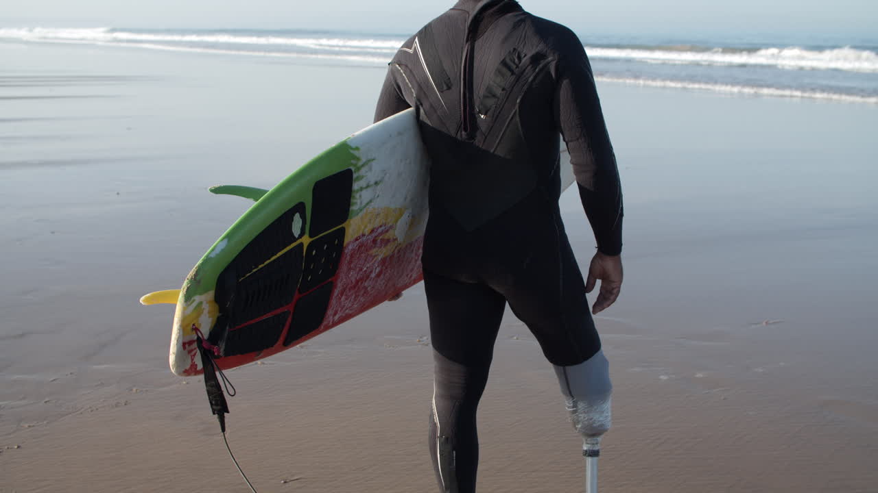 Premium stock video - Back view of a male surfer with artificial leg ...
