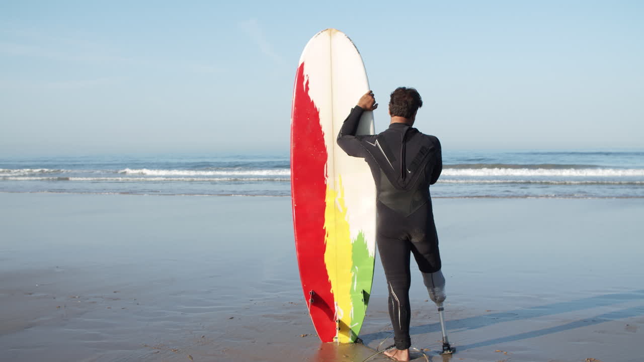 Premium stock video - Back view of a male surfer in wetsuit leaning on ...
