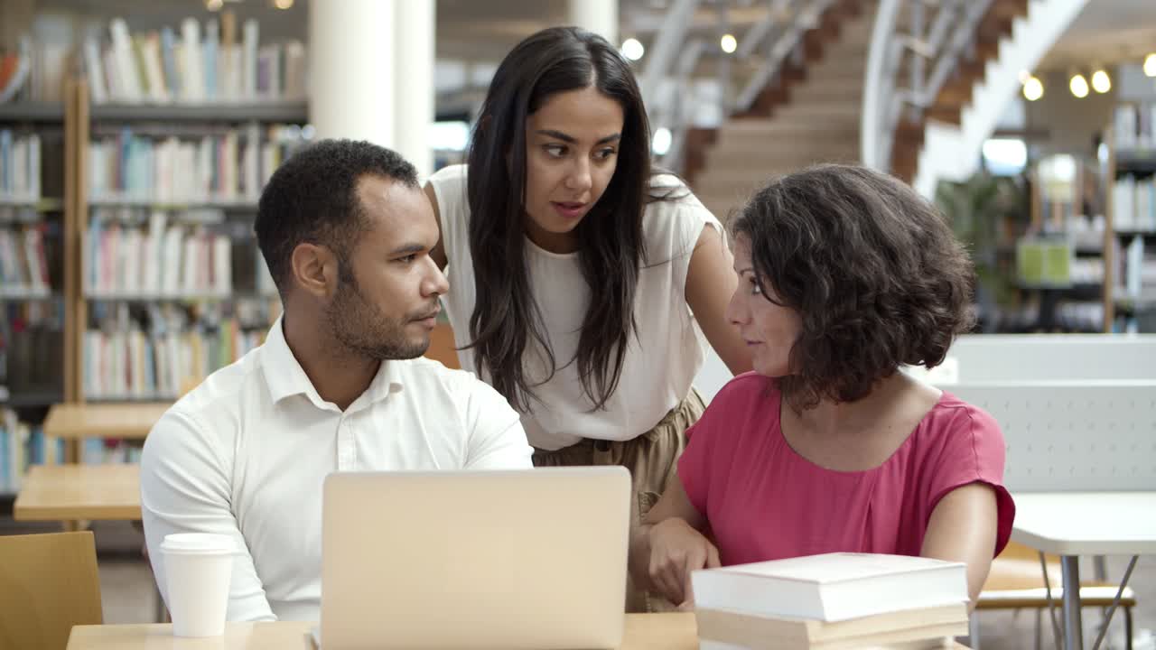 Free stock video - Serious students sitting at table in library with laptop