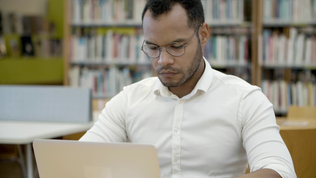 Free stock video - Focused young man working with laptop in library