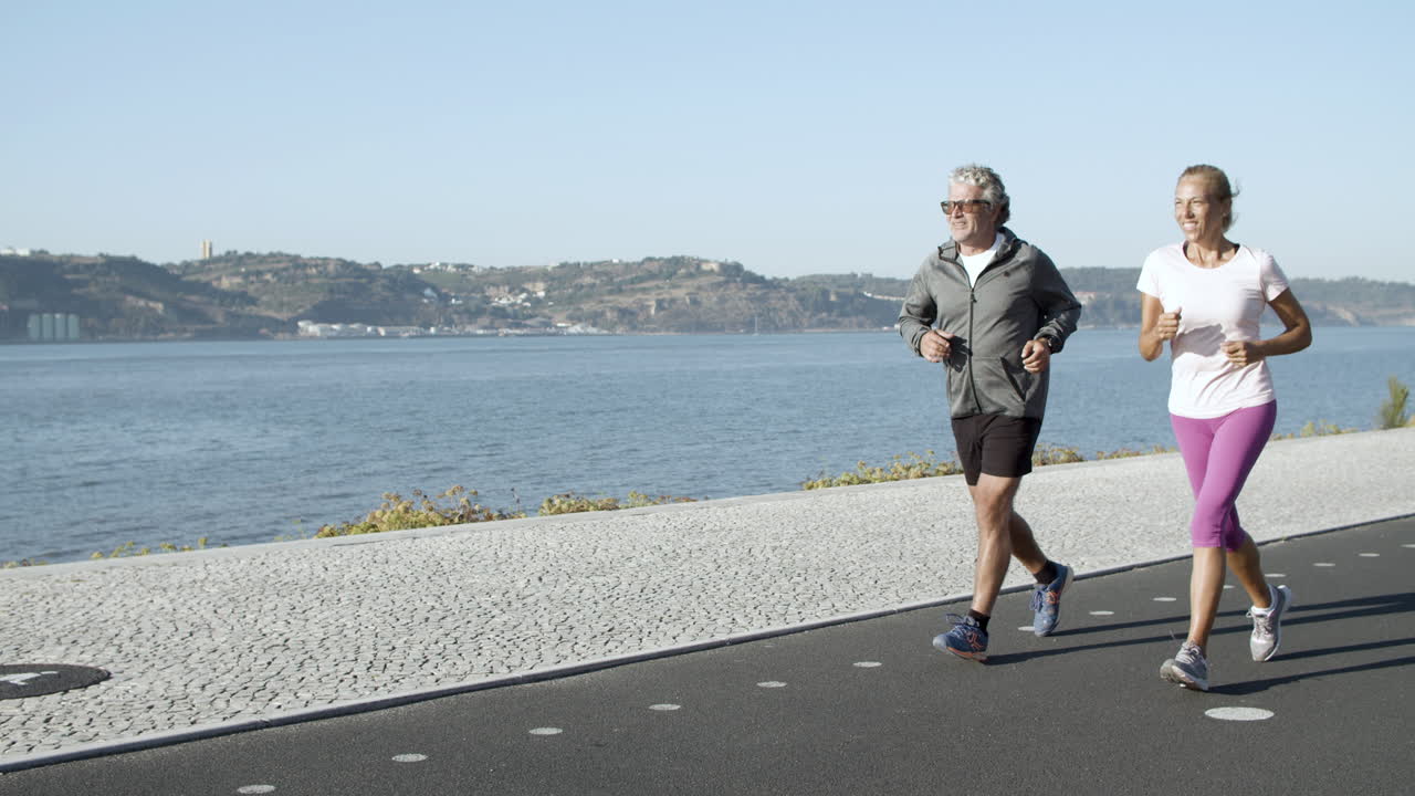 Free stock video - Active man and woman jogging on asphalt road along sea