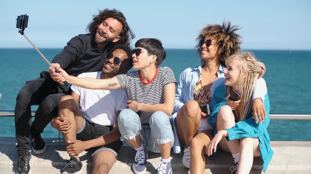 Premium stock video - Laughing friends taking selfie on seafront
