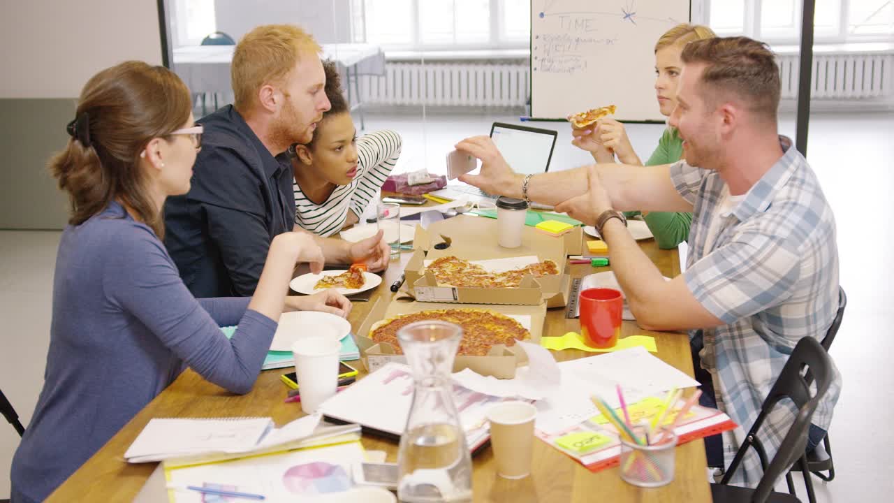 Premium stock video - Colleagues eating pizza at office table