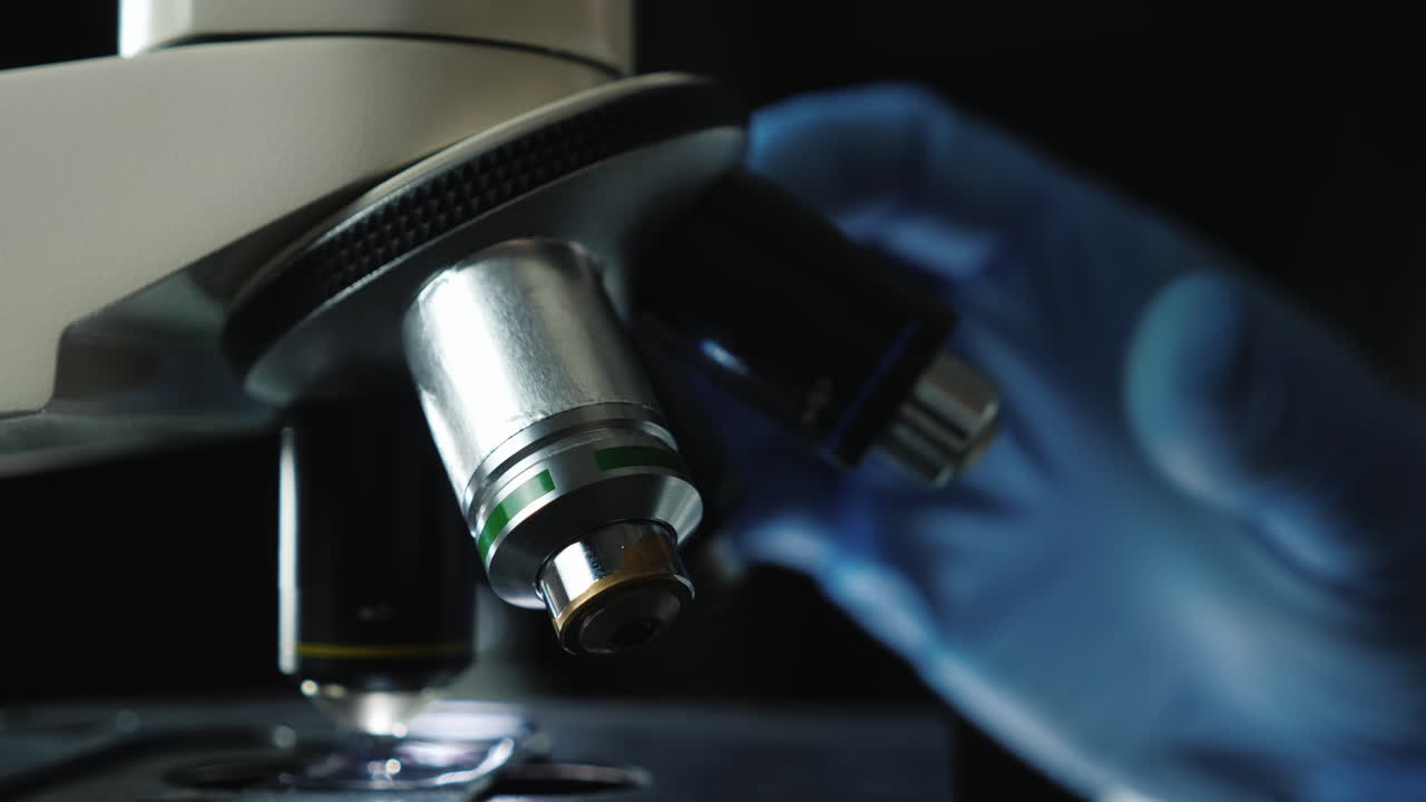 Premium stock video - Hand in glove turns microscope lenses