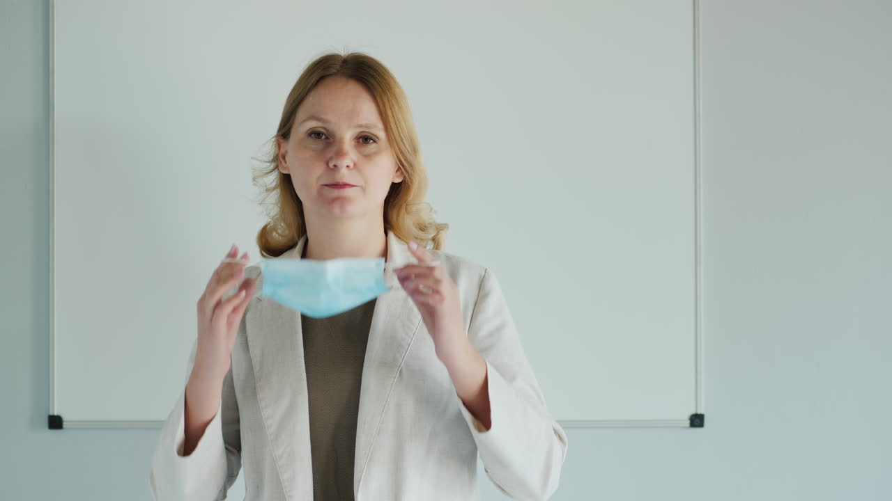 Premium stock video - Teacher wears protective mask in front of classroom