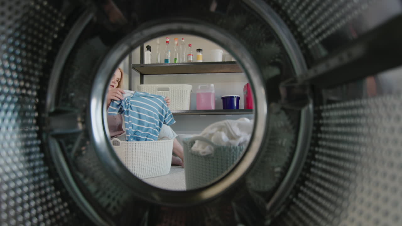 Premium stock video - A tired woman throws clothes into the washing machine