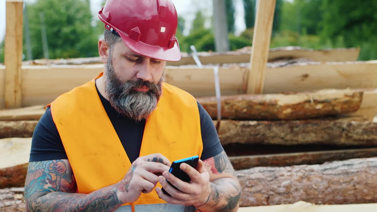 Premium stock video - A bearded builder in a helmet uses a smartphone