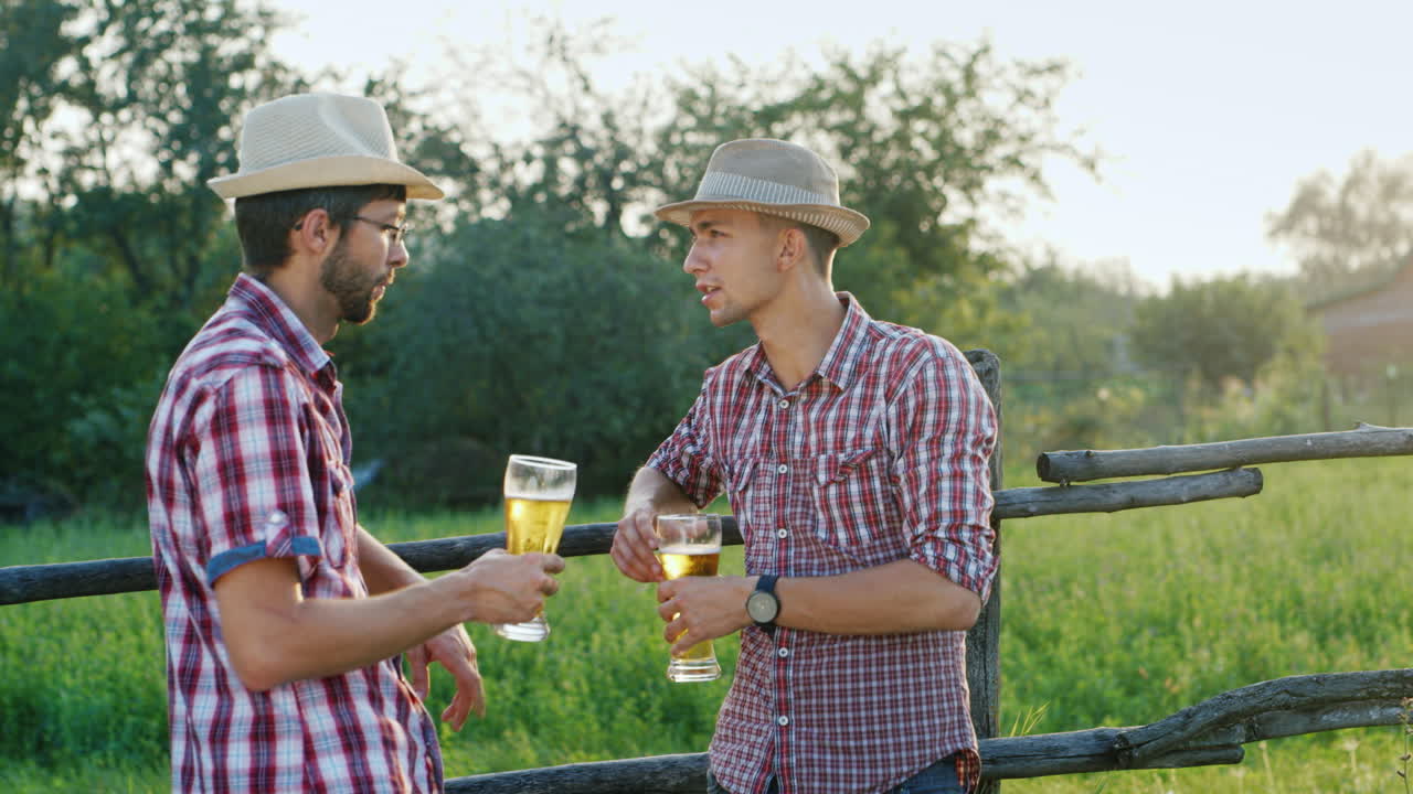Premium stock video - Two farmers drink beer at a fence of their ranch