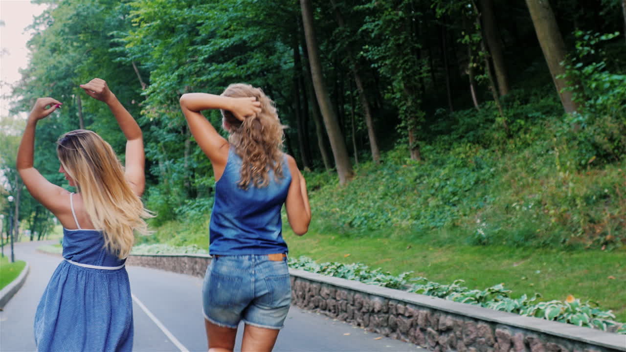 Premium stock video - Carefree young women walk down the road in the park