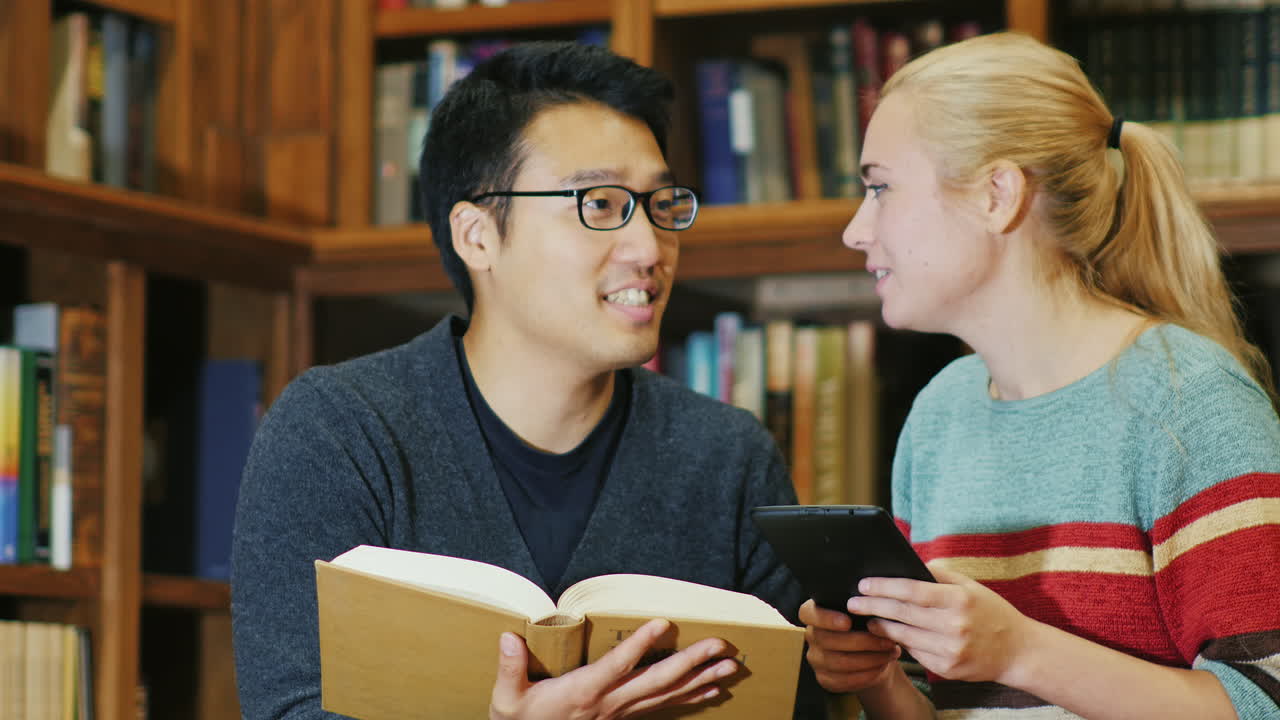 Premium stock video - Smiling korean man talking to a woman in the library