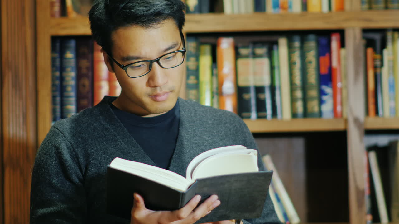 Premium stock video - Good looking asian man in glasses reading a book ...