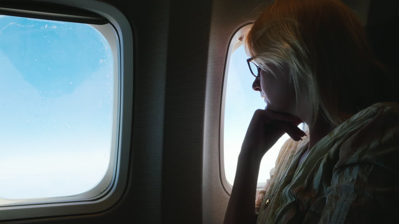 Premium stock video - A pensive woman flies in an airplane looks out ...